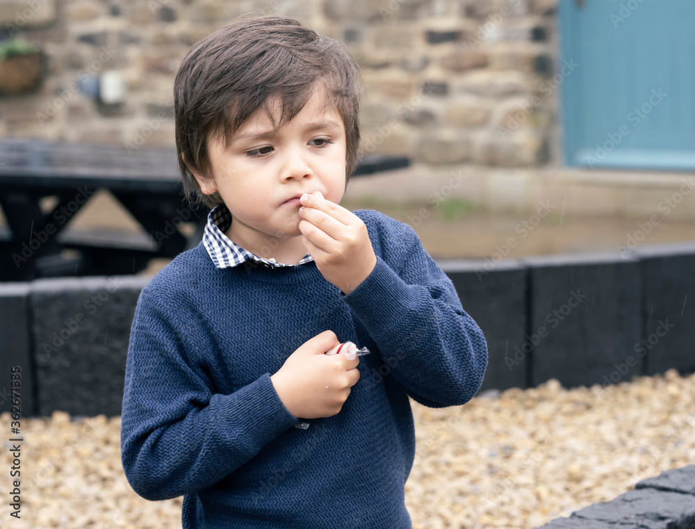Side view of English boy eating a candy with rain drops on his hair in ...