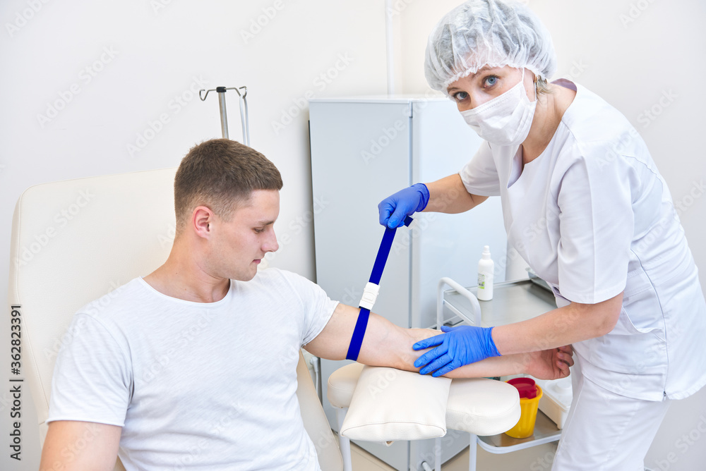 man in medical office gives blood. doctor puts tourniquet on his arm ...