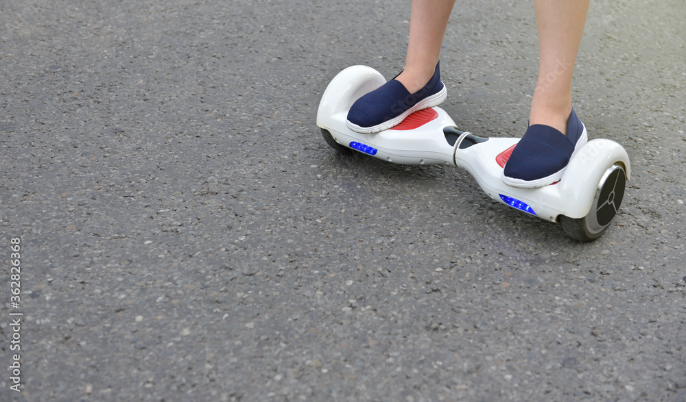 Electric hoverboard and legs of a teenage girl in blue shoes on asphalt ...