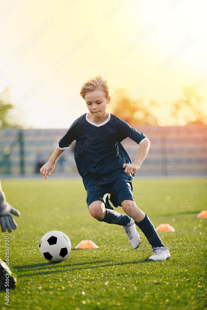 Young blonde boy kicking soccer ball on drill. Kids playing football ...