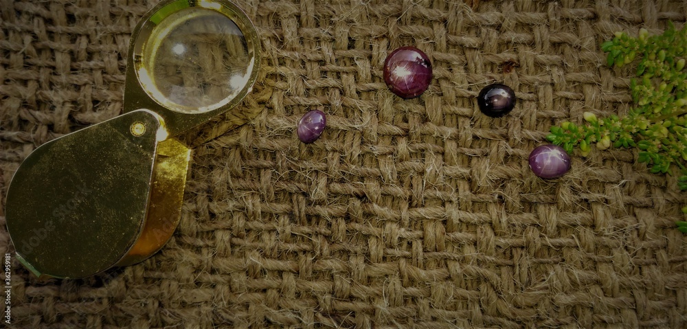 On a jute cloth, a gem loupe and different types of precious gemstones ...