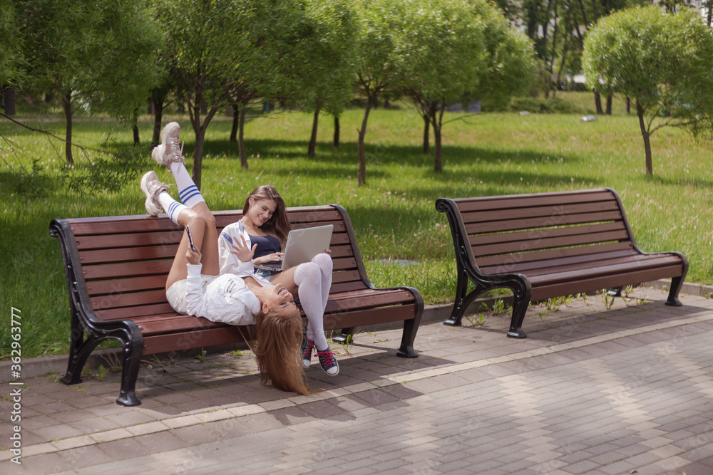 Two blonde girls with long hair in short shorts are walking in the park ...