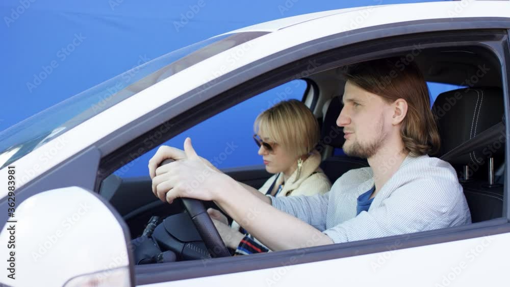 Two people are sitting in a car and talking. Brunette guy is driving ...