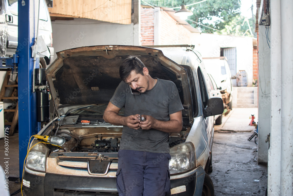 mechanic leaning against a car while making a call with his cell phone ...