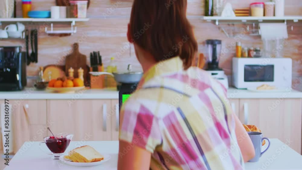 Woman looking at laptop with green mock up while drinking coffee in ...