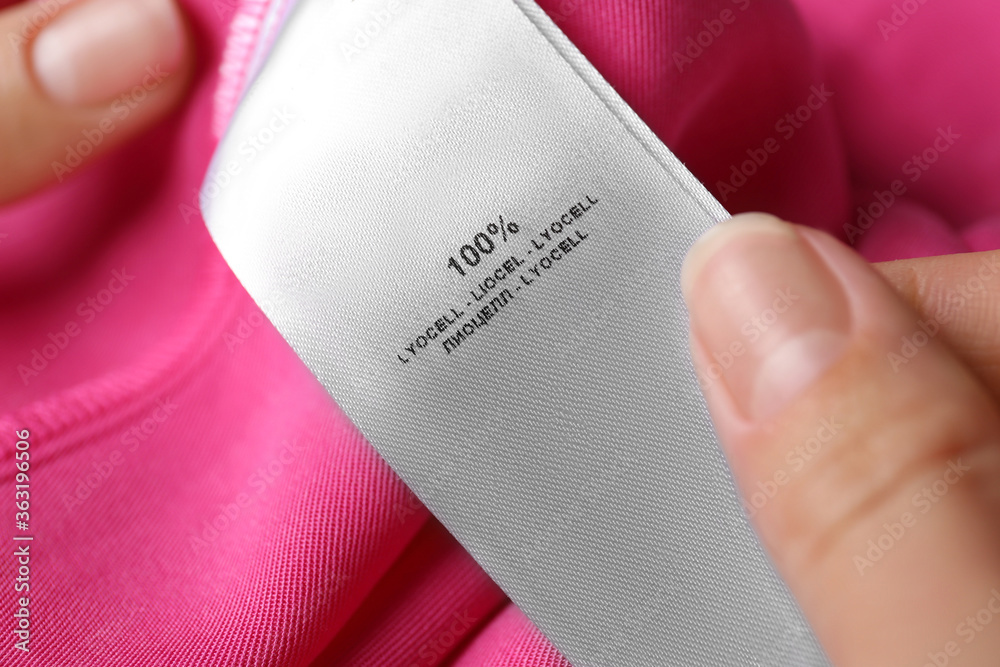 Woman reading clothing label with material content on pink shirt ...