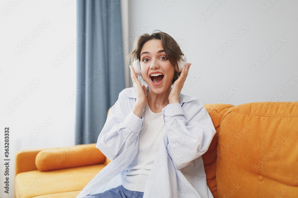 Excited young woman girl in white casual clothes sit on couch spending ...