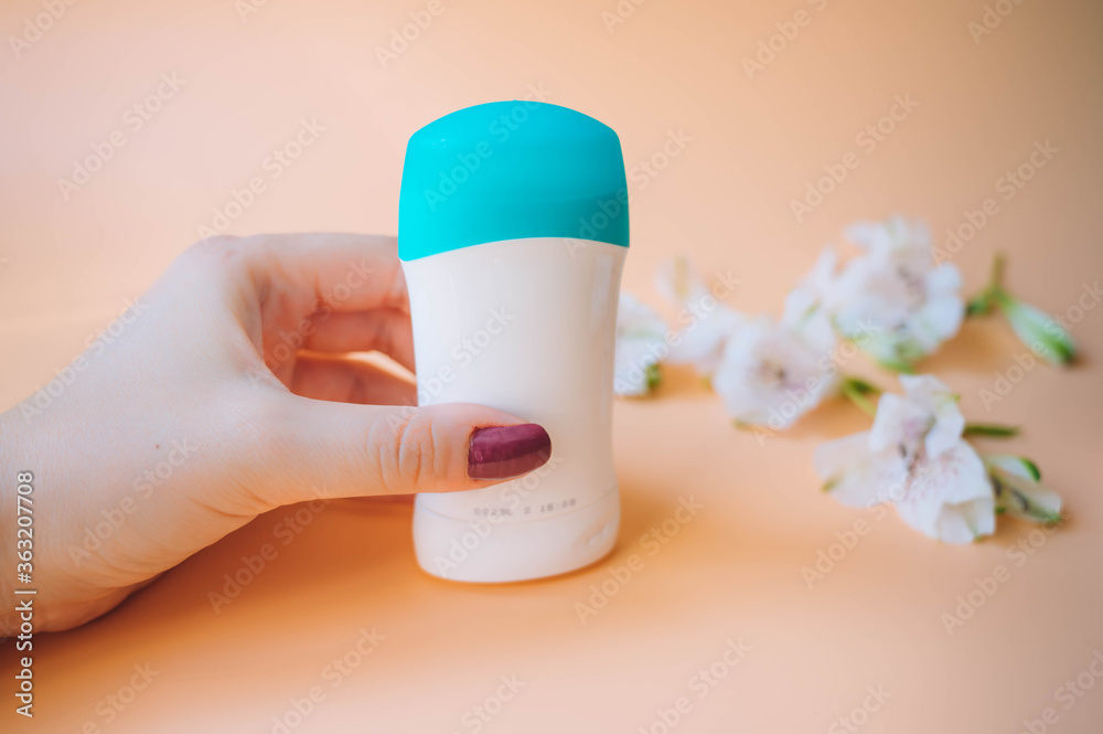 Female hand holding dry deodorant in a white bottle on a bright ...