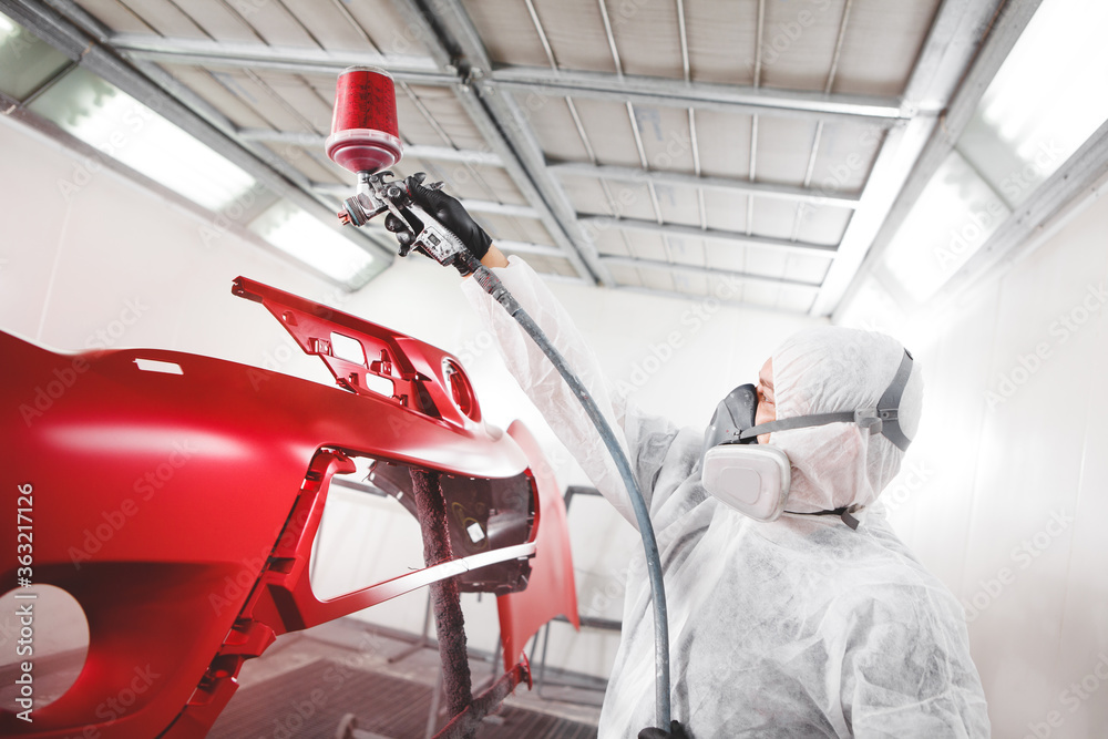 Auto mechanic worker painting car element with spray gun in a paint ...