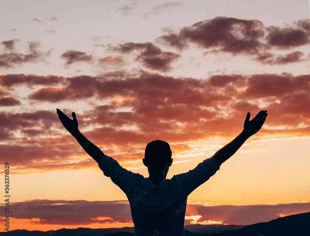 Young man rising up the hands and greeting the stunning sunset orange ...