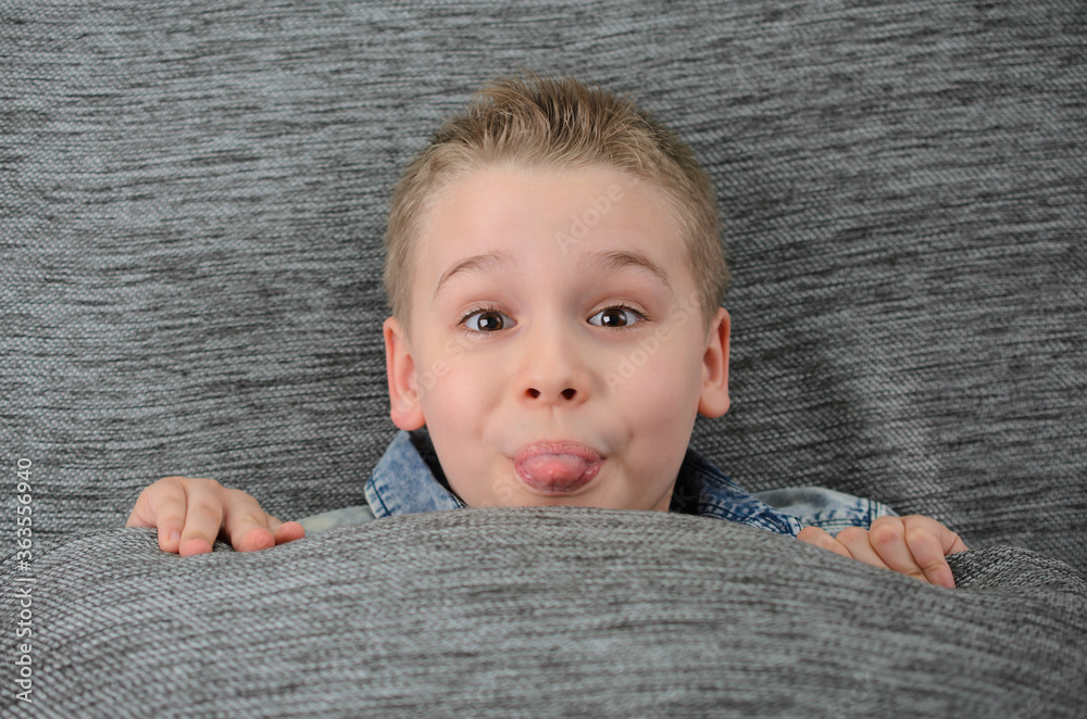 Cute funny boy is lying his backs on couch and making funny face ...