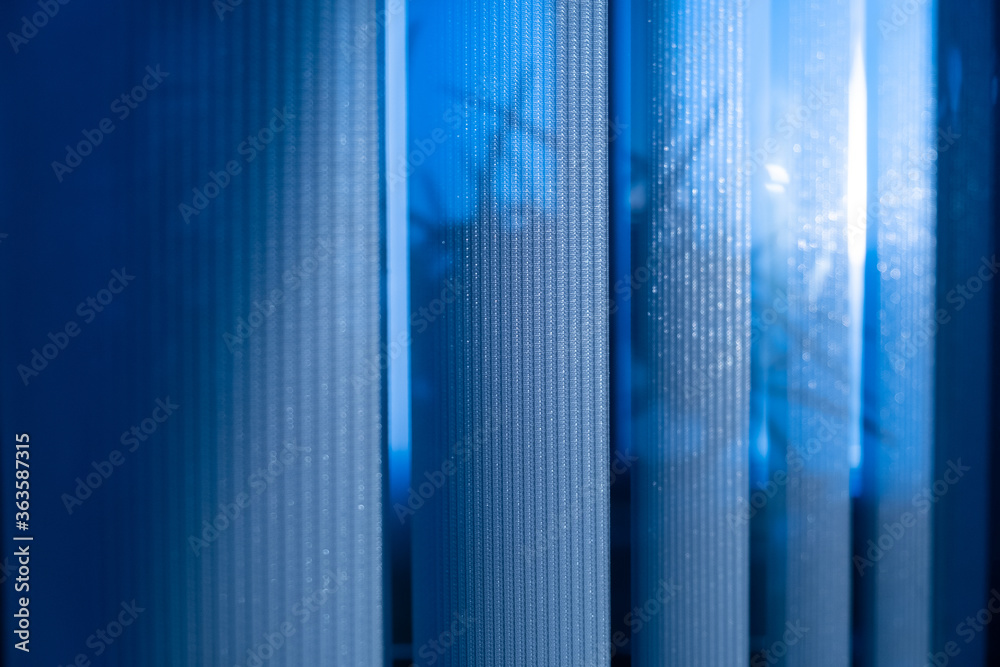 Vertical wide blinds outside the window in the light of the sunset, a ...