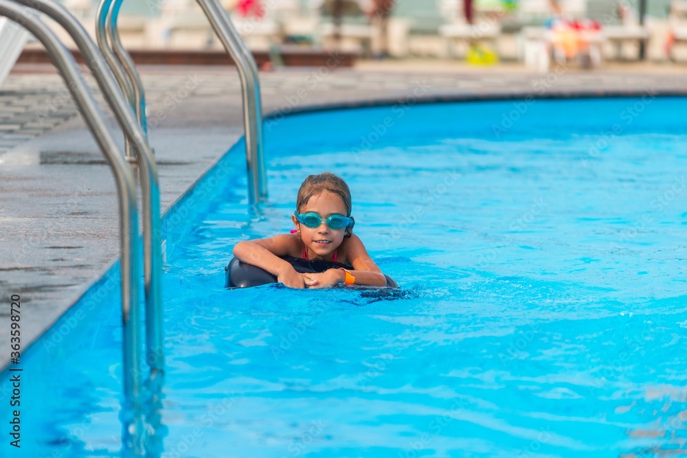 Charming little girl in swimming goggles and a lifebuoy swims in the ...