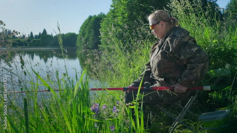 Woman fishing. Elderly angler woman fishing on the calm summer pond ...