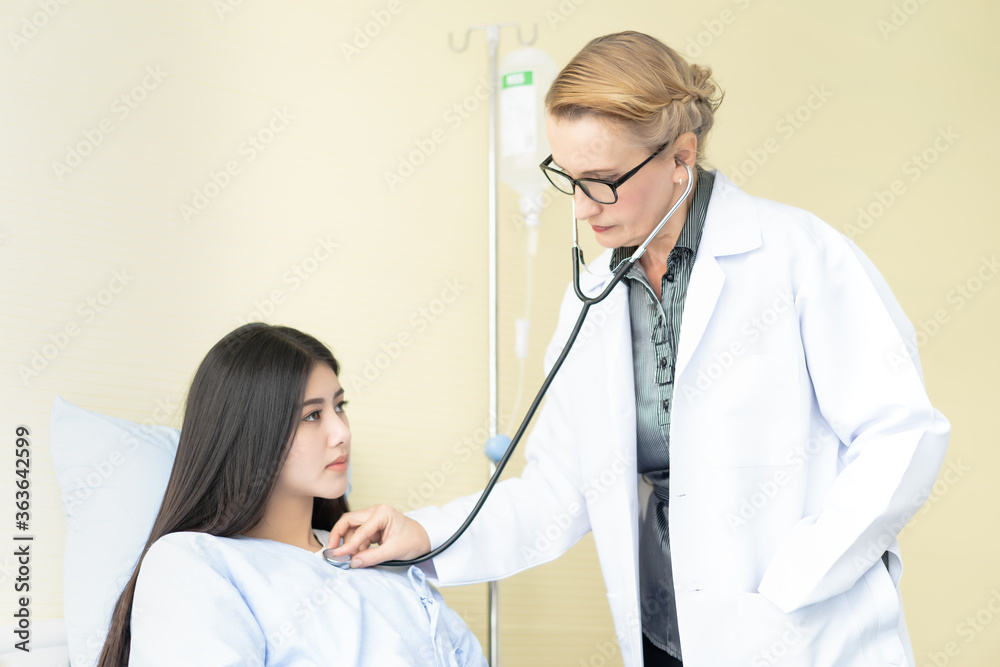 Senior female doctor checking heart beat of patient in hospital bed ...