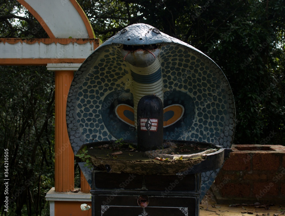 Statue of a big snake in front of a temple. The Siva-lingam is seen in ...
