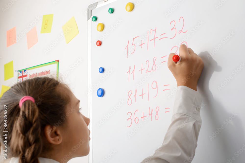 Schoolgirl calculating figures on the whiteboard, having lesson of math ...