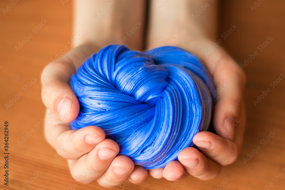 The child plays with a home made blue toy slime. The girl made a heart ...