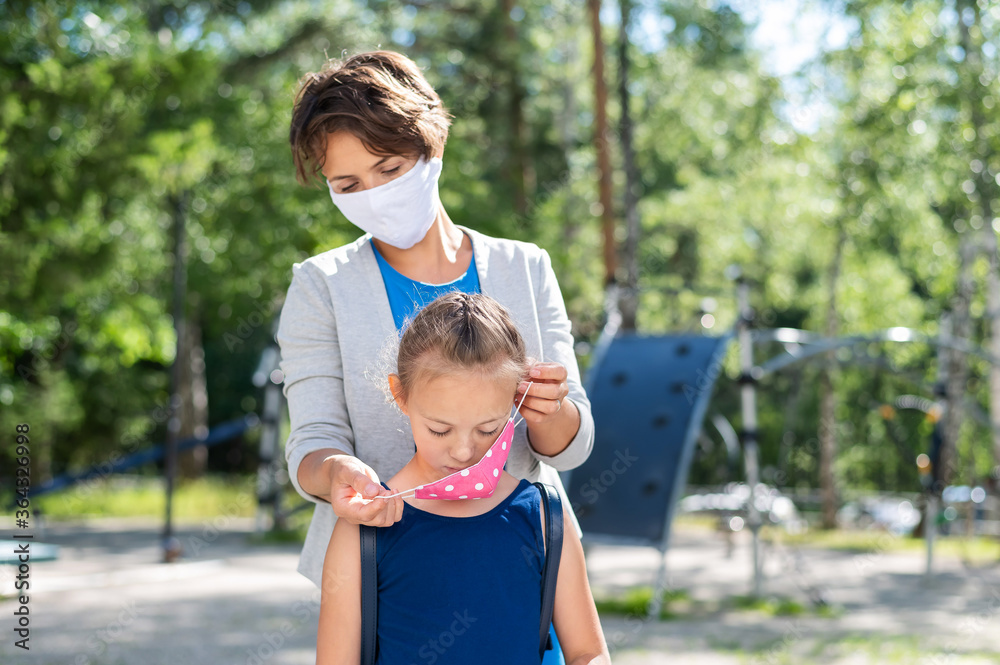 Caucasian woman puts a protective mask on her daughter outdoors. Caring ...