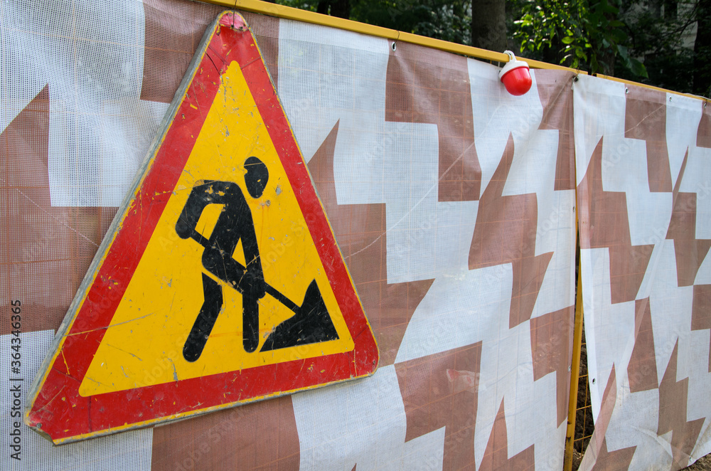 A triangular road sign "Roadworks" located on a temporary textile fence ...