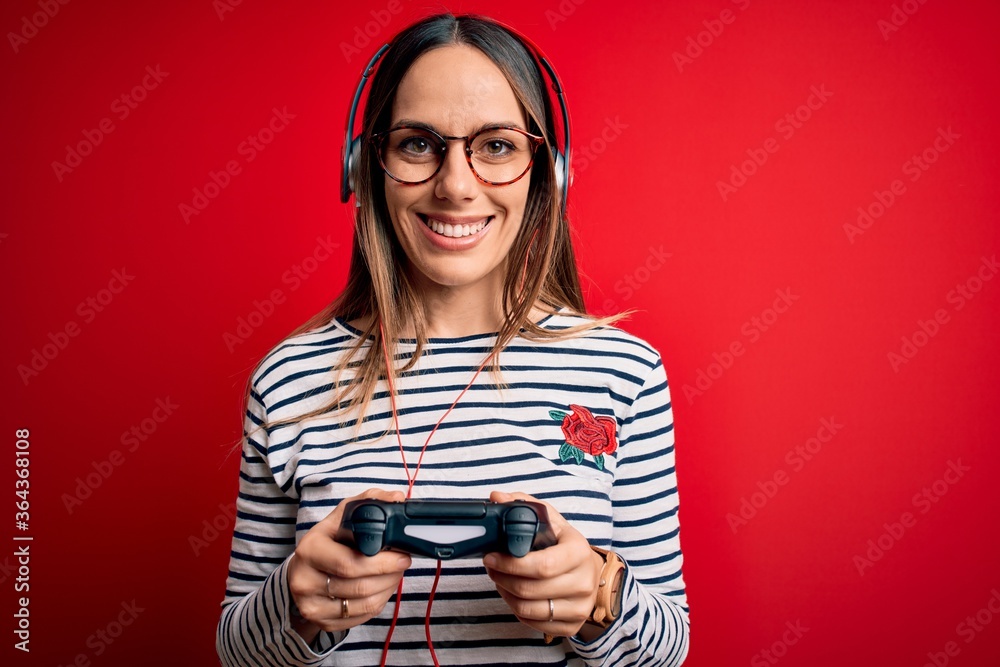 Young blonde gamer woman using gamepad playing video games over red ...