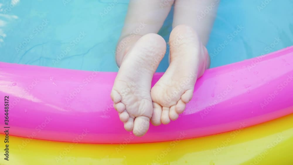 Kids feet laying on colorful rainbow inflatable swimming pool. Young ...
