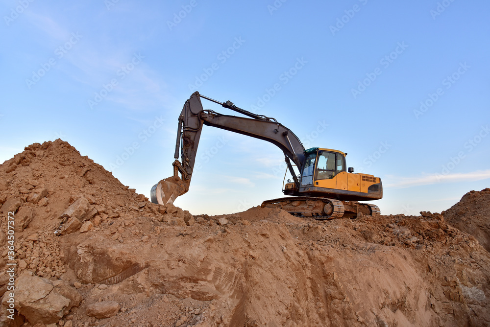 Yellow excavator during earthmoving at open pit on blue sky background ...