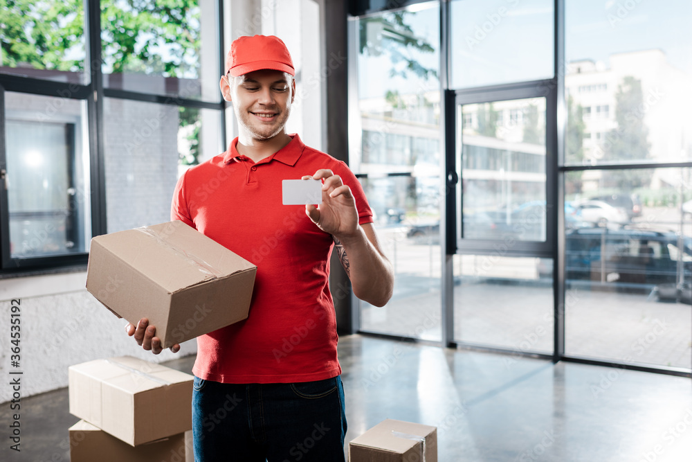 happy delivery man in cap holding blank card and carton box Stock Photo ...