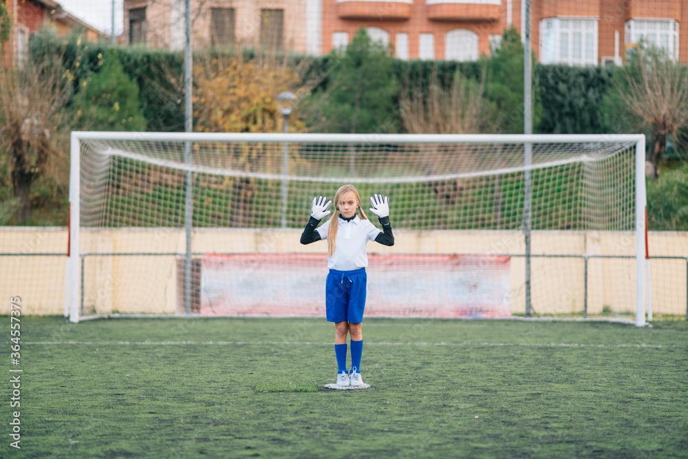 Serious preteen girl keeper in white and blue uniform defending soccer ...