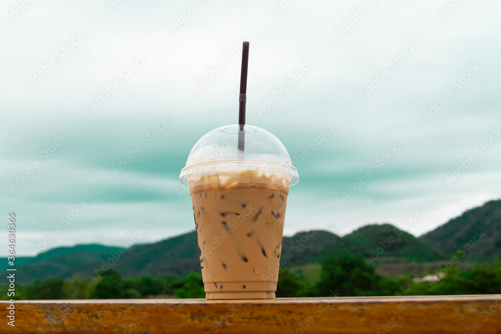 Iced coffee in a glass Resting on a long table Which has a scene in the ...