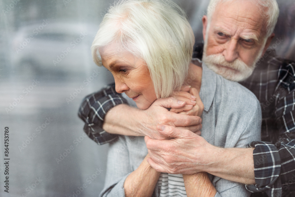 upset senior man hugging wife, sick on dementia, while standing by ...