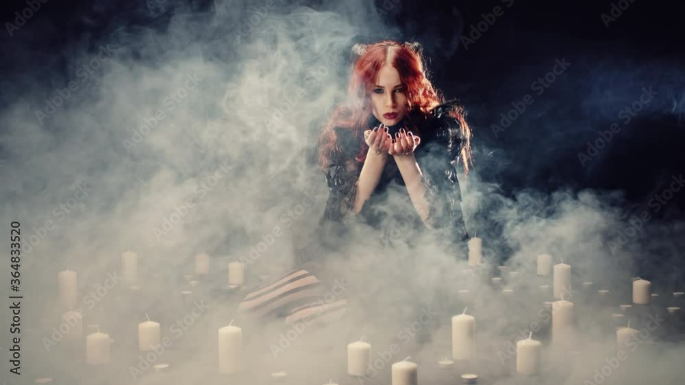 Young red-haired girl with devil horns and in black suit in dark room ...