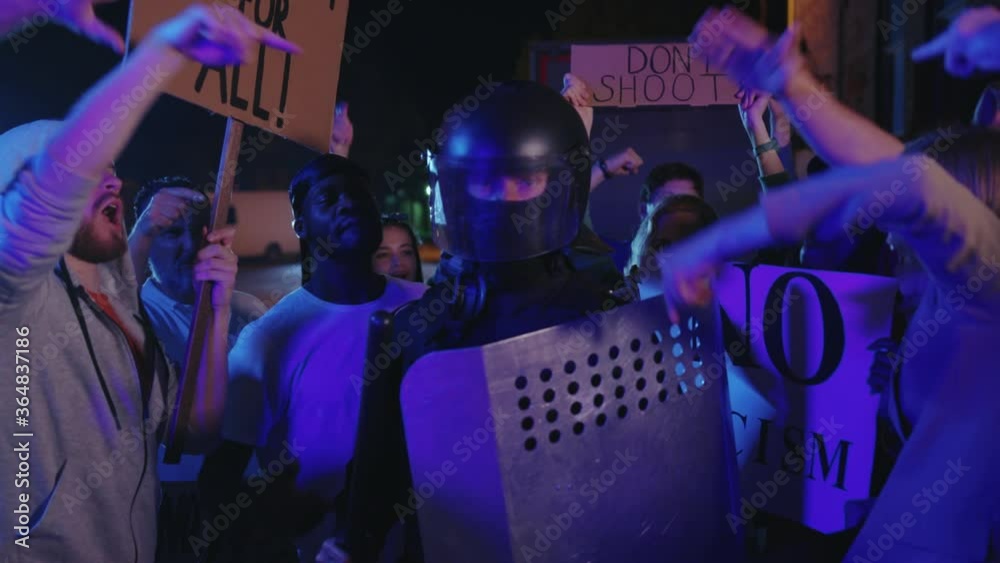 Portrait strong and armed police officer standing among shouting people ...
