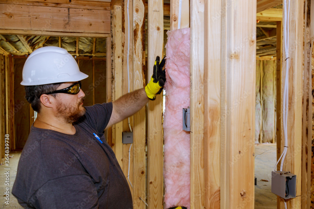 Construction worker installing thermal insulation layer under the wall ...