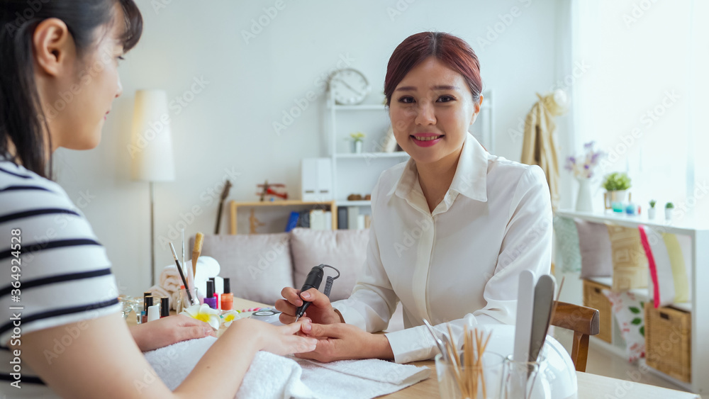 young asian chinese female beautician polishing fingernails of lady ...