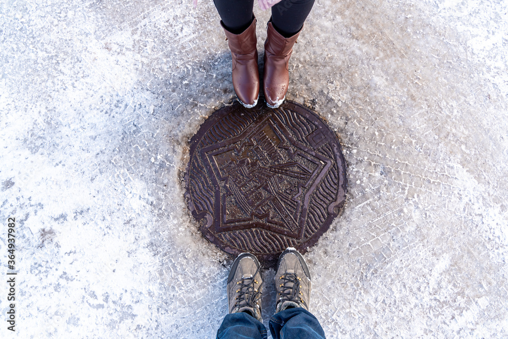 Traveler feet standing on manhole drain cover on the street in winter ...