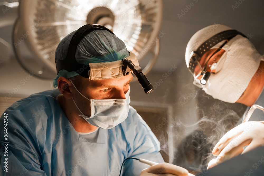 2 surgeons with headlamp do plastic operation in medical clinic. Chest ...