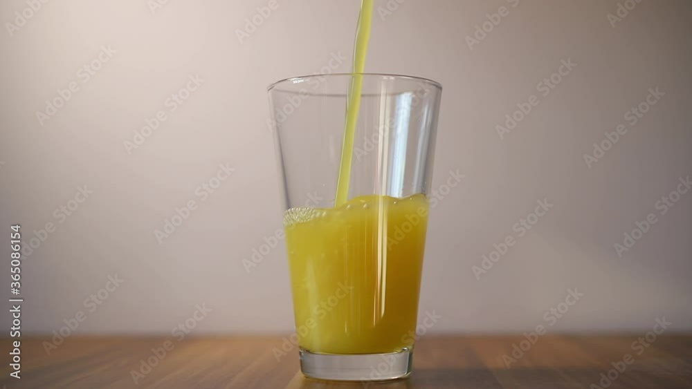 Close-up of a glass cup pouring orange juice from a decanter on a white ...