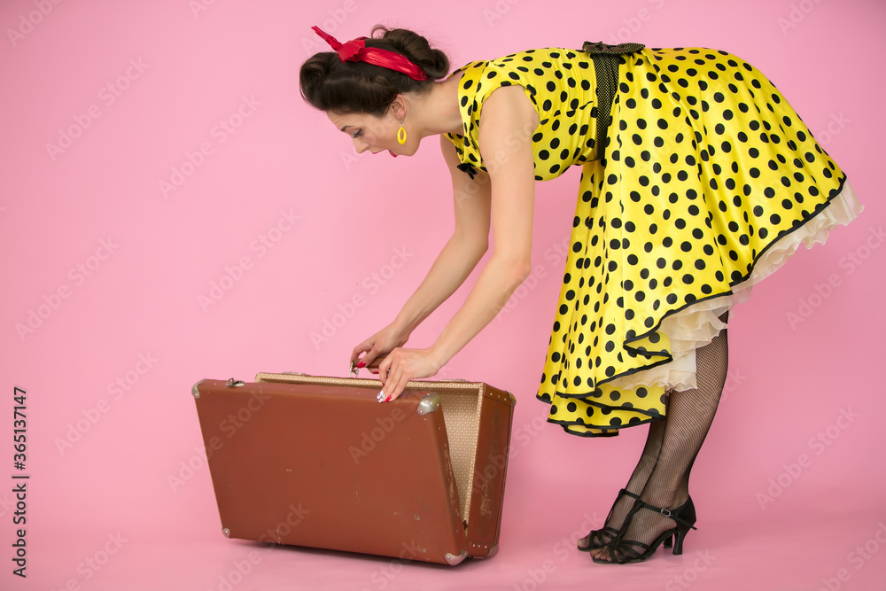 Beautiful pin-up girl opens a suitcase. Retro woman in yellow polka dot ...