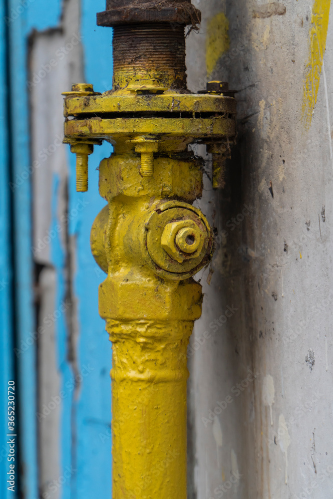Old yellow gas valve, flange and screws on vertical pipe near wall ...