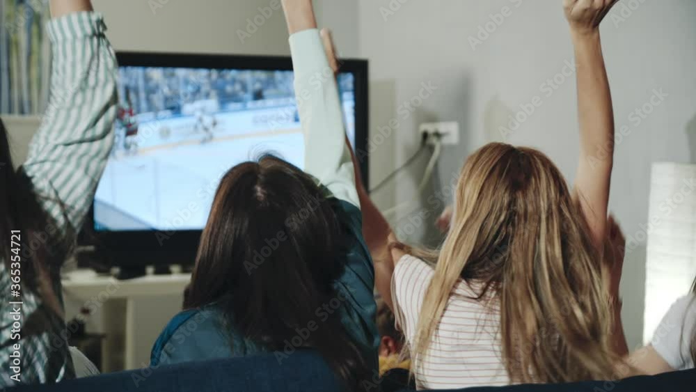 Backshot group of teens watching hockey match on tv celebrating goal ...