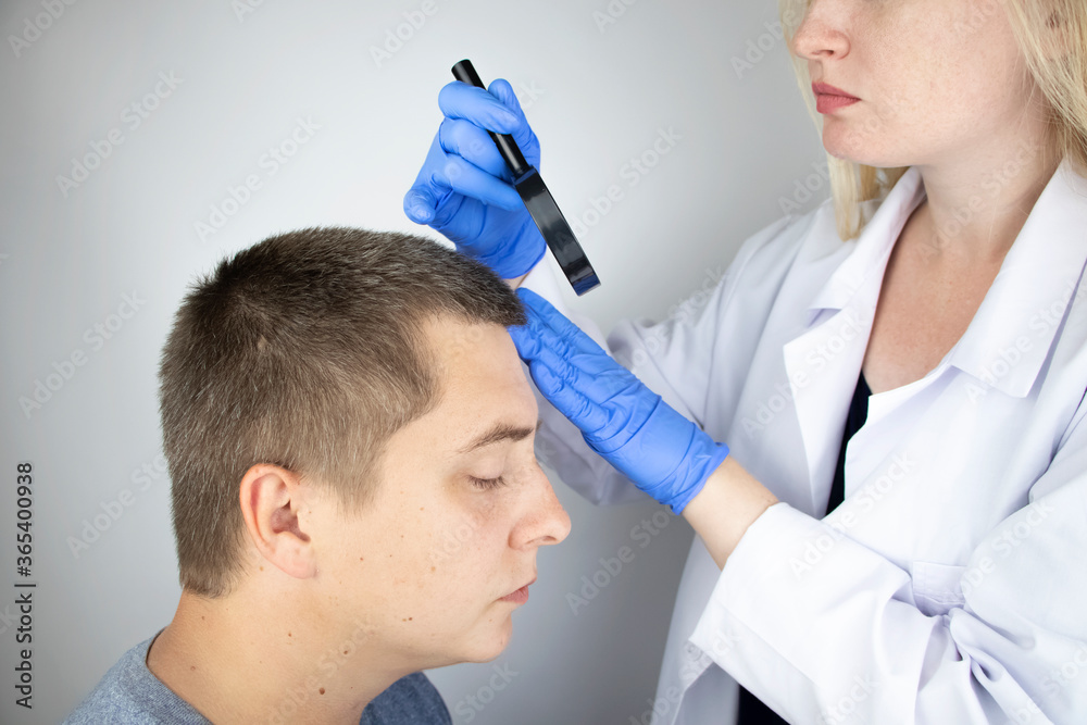 A trichologist examines the hair of a man who begins alopecia ...