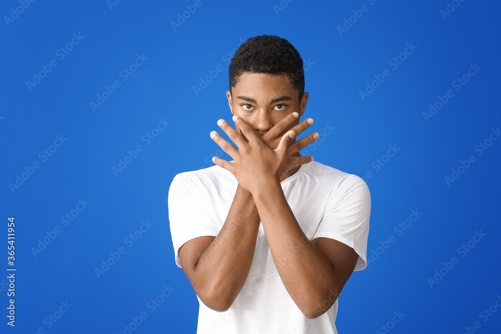 Sad African-American teenage boy covering his mouth on color background ...