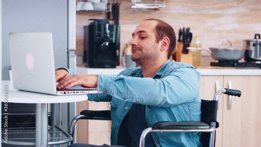 Man with special needs in wheelchair working on laptop in kitchen ...