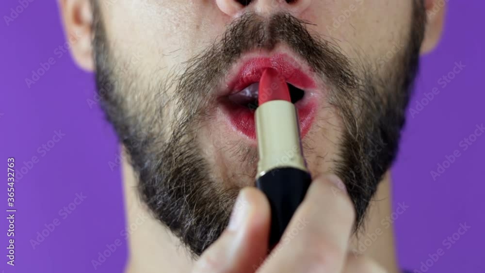 A young guy with a beard paints his lips with red lipstick. Close-up of ...