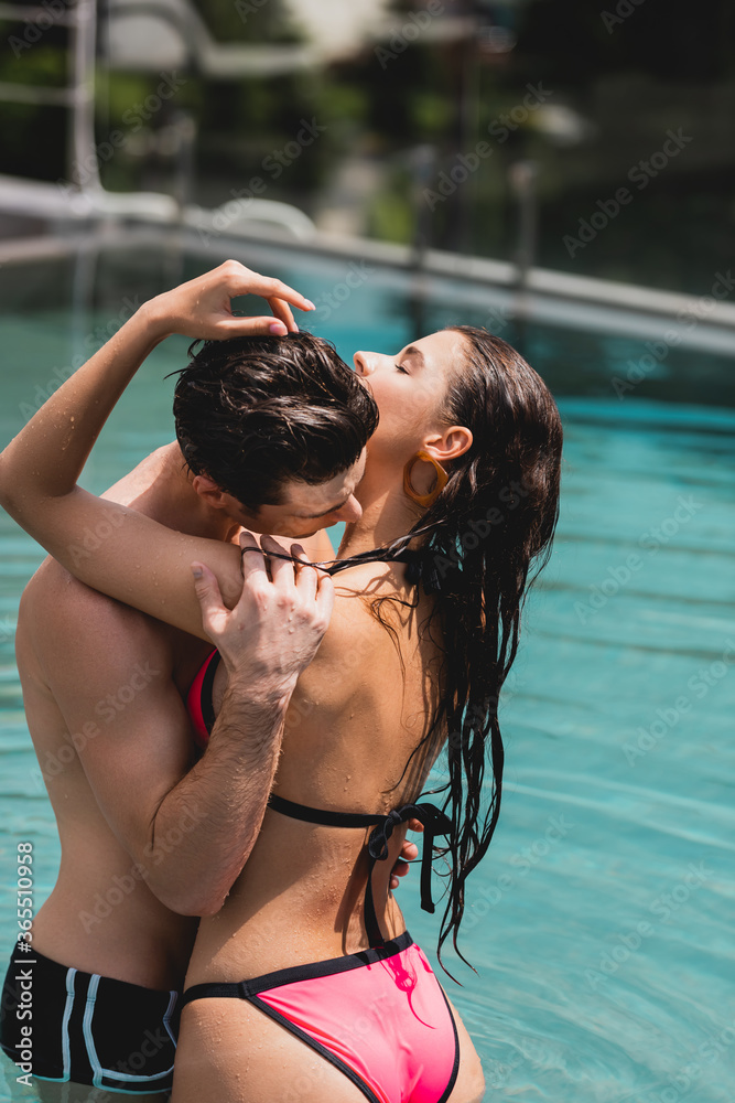 Shirtless Man Kissing Sensual Girl In Swimsuit Standing In Pool Stock