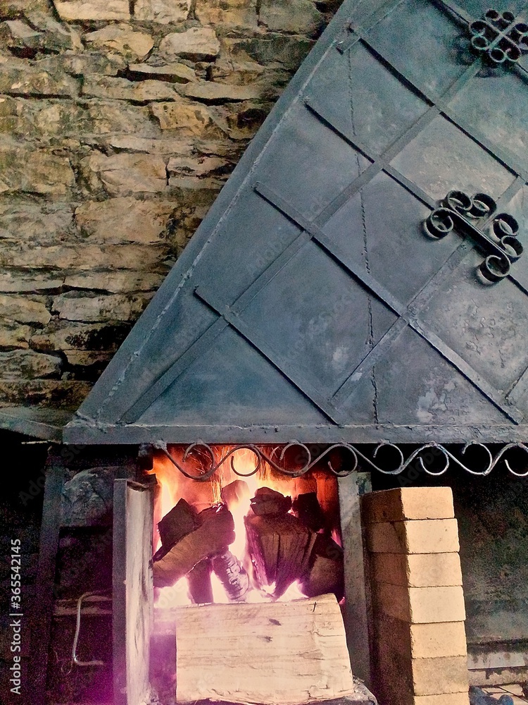 fire from burning firewood in a stone stove with a metal canopy near a ...