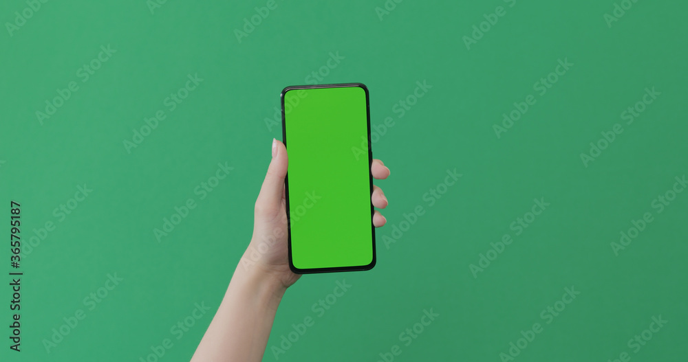 Young female hand hold smartphone with green screen on green background ...