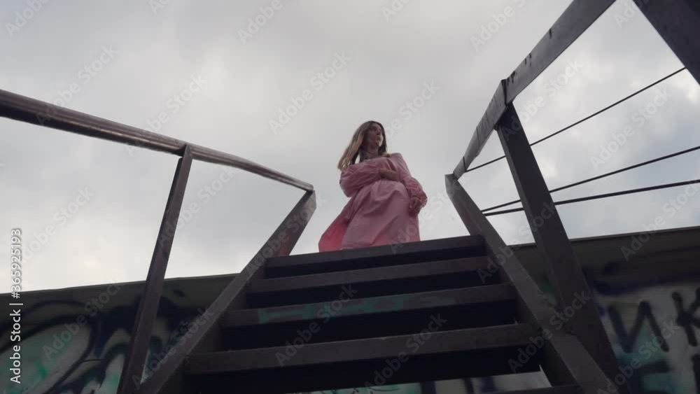 girl, model in a pink dress at the top of a metal, rusty staircase ...