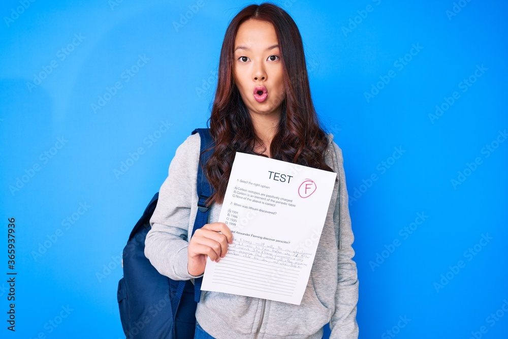 Young beautiful chinese girl showing a failed exam scared and amazed ...